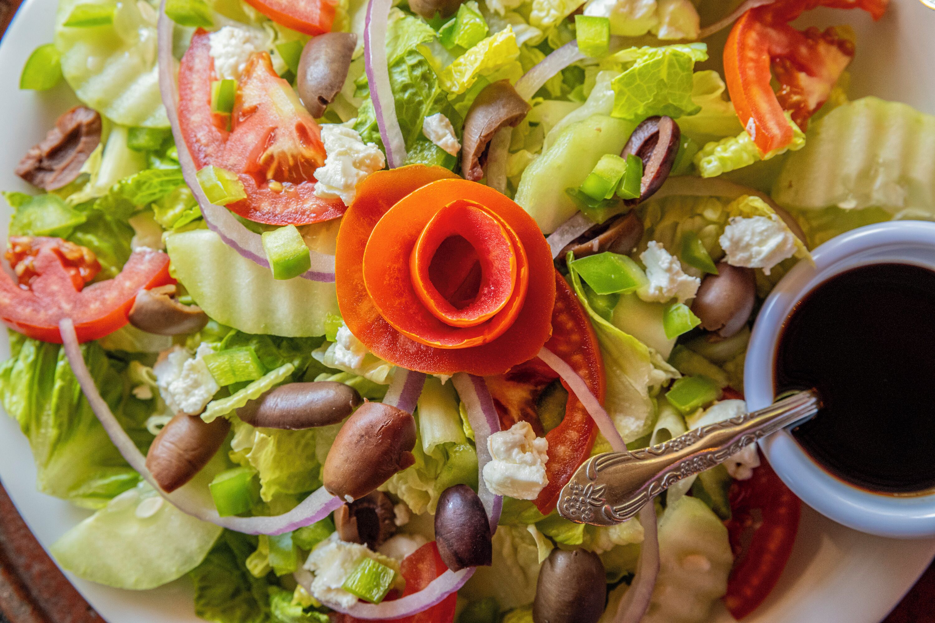 Salada com diversos vegetais e uma rosa decorativa, acompanhada de uma pequena tigela de molho.