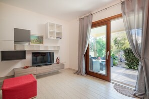 Uma sala de estar moderna com uma TV de tela plana, um banquinho vermelho e uma porta de vidro deslizante que dá para um pátio com móveis externos.