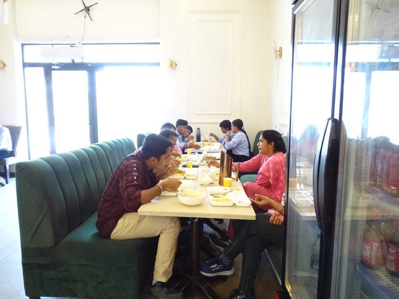 Um grupo de pessoas jantando à mesa em um ambiente com sofá verde e divisória de vidro.