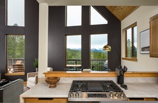Uma cozinha moderna com uma ilha grande, fogão a gás e vista para montanhas através de amplas janelas.