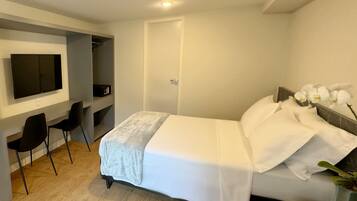 Quarto de hotel com cama, secretária e cadeira, televisão e porta.