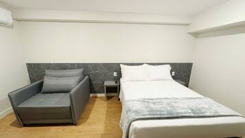 Quarto de hotel com cama, sofá cinzento, mesa de cabeceira e cabeceira de mármore.