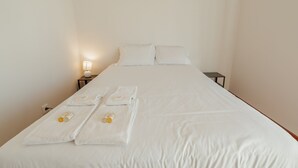 Cama bem arrumada com lençóis e toalhas brancas, um abajur e uma mesinha de cabeceira com uma garrafa e um copo.