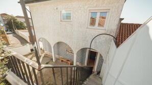 Um edifício residencial com uma escadaria que leva a uma varanda, uma pequena janela e uma porta.