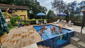 Uma área de piscina com deck ladrilhado, espreguiçadeiras e guarda-sóis.