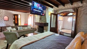 Um quarto aconchegante com uma cama, um sofá, uma TV e uma parede de pedra.