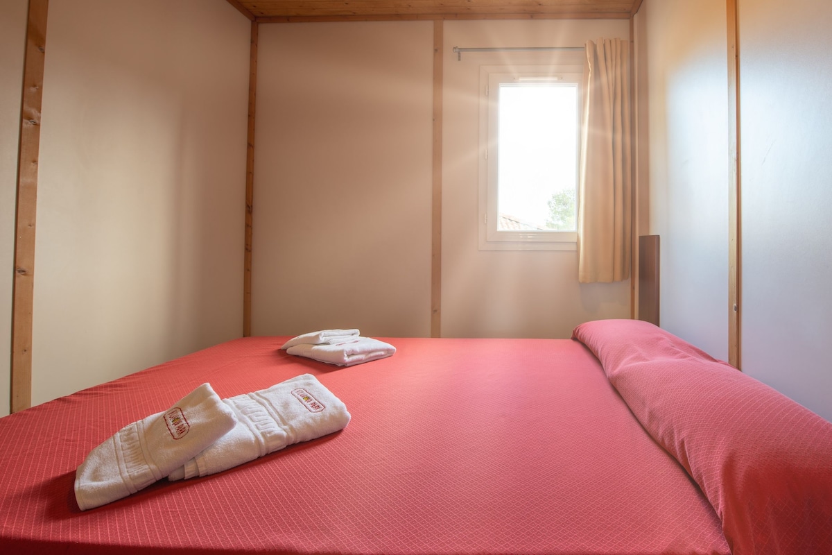Uma cama de solteiro com colchão vermelho e roupa de cama branca, incluindo uma toalha dobrada e um cobertor.