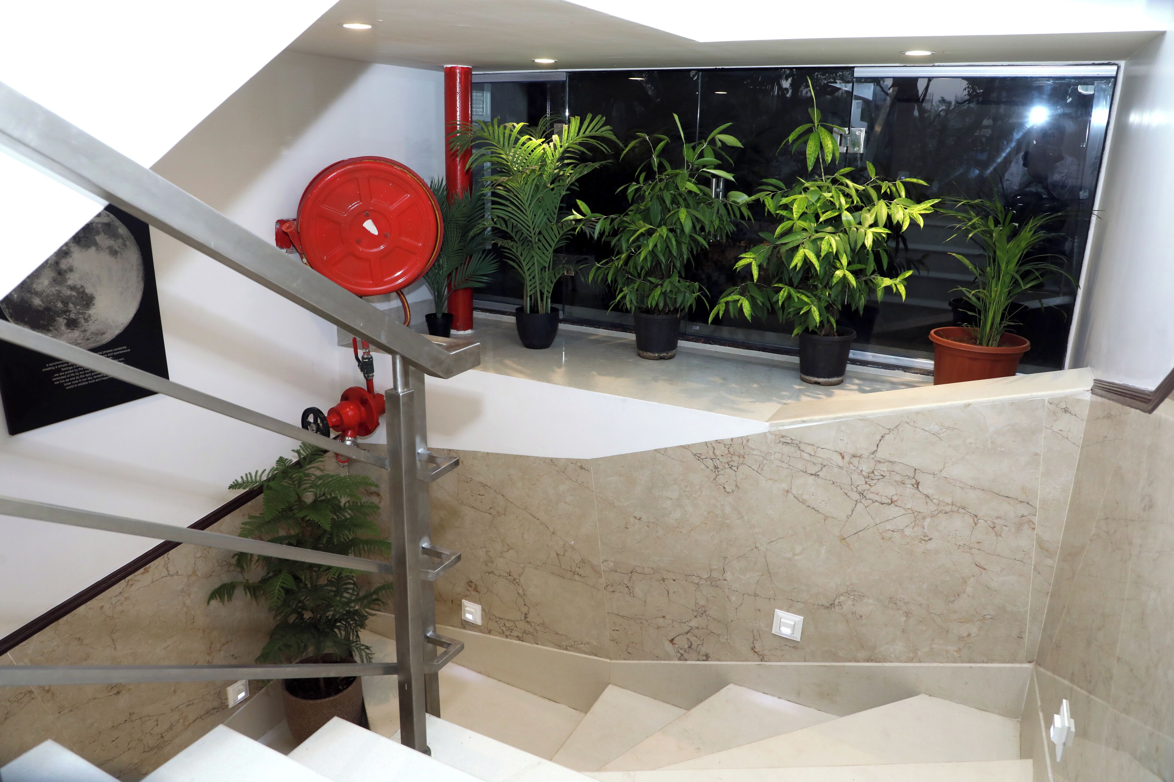 Interior moderno com escadaria de mármore, plantas em vasos e alarme de incêndio vermelho.