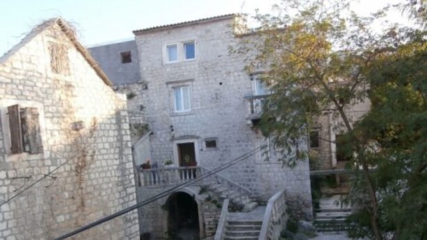 Edifício de pedra com escadaria que leva a uma porta, rodeado de vegetação.
