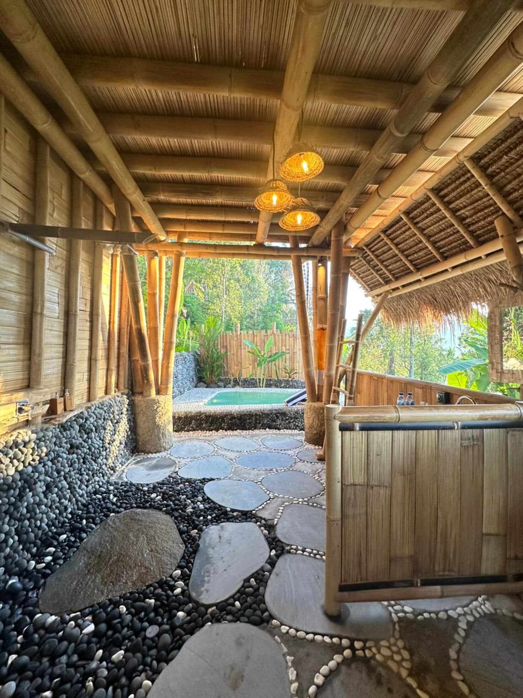 Uma área de spa com hidromassagem, caminho de pedra, paredes de bambu e telhado de palha.