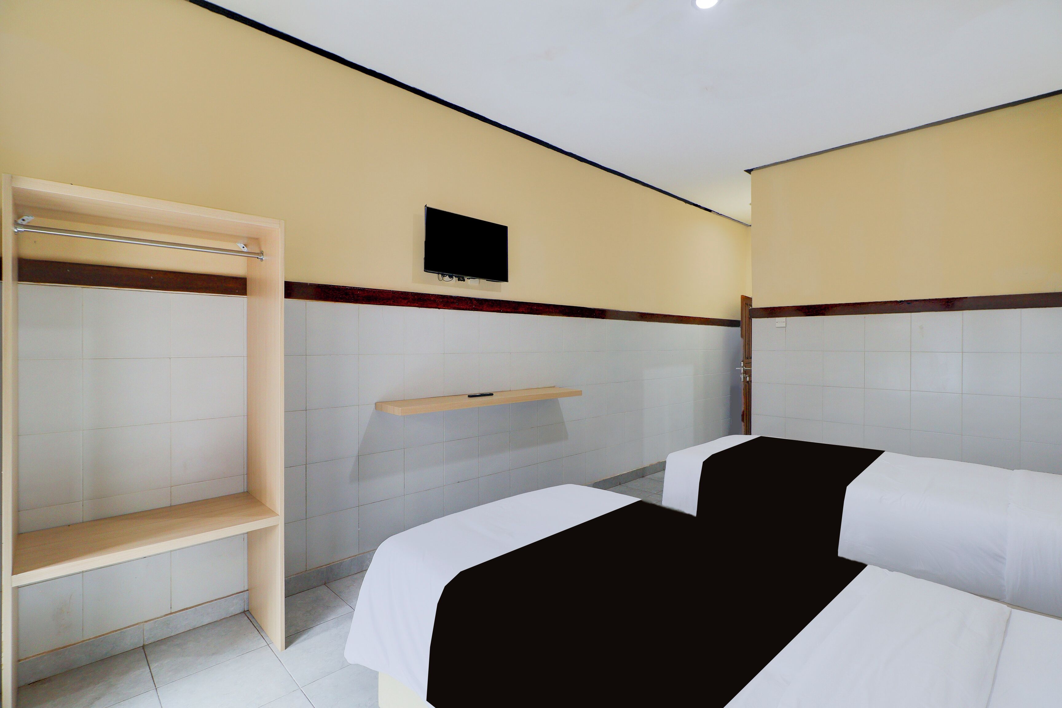 Quarto de hotel com duas camas, uma TV fixada na parede e uma prateleira de madeira.