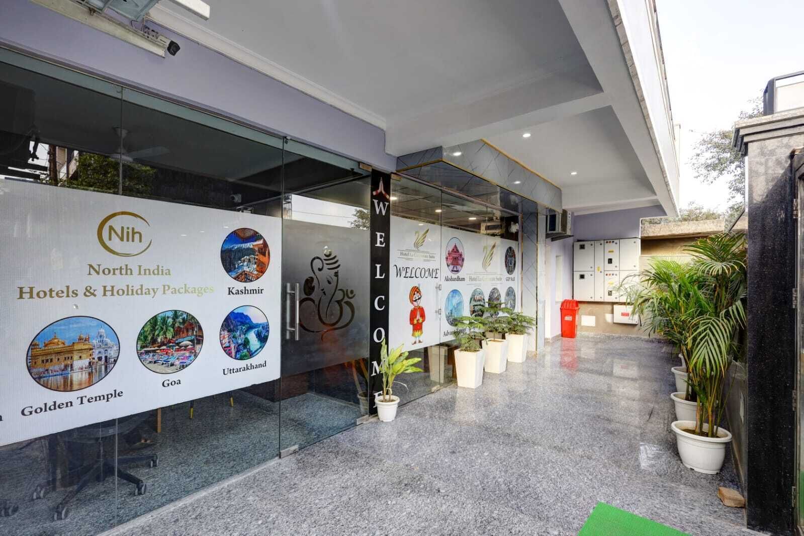 Entrada de um hotel com fachada de vidro, placa de boas-vindas e plantas em vasos.