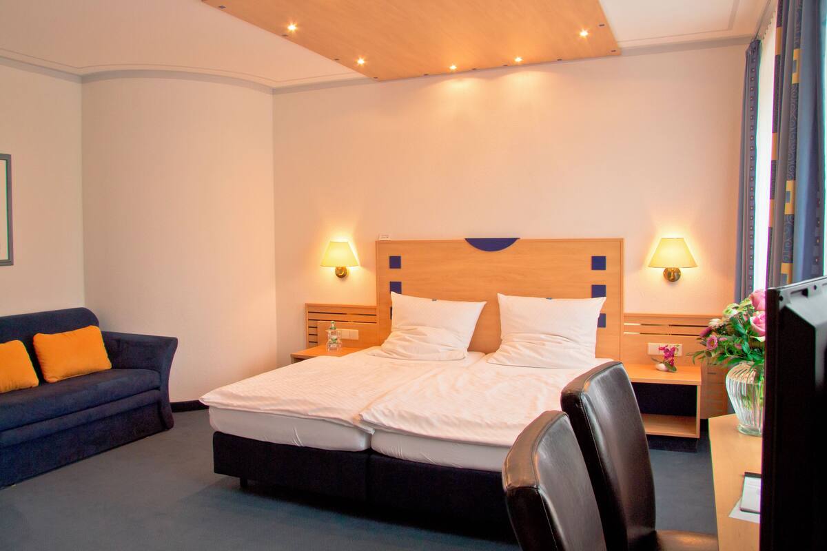 Quarto de hotel com uma cama, um sofá, uma escrivaninha e uma cadeira.