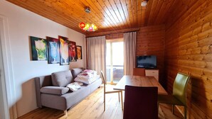 Quarto com painéis de madeira, um sofá, uma mesa de jantar e uma televisão.