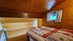 Um quarto de cabana de madeira com uma cama, uma mesa pequena e uma janela com cortinas.
