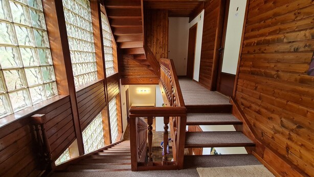 Uma escada de madeira com corrimão, degraus carpetados e uma pequena mesa na base.