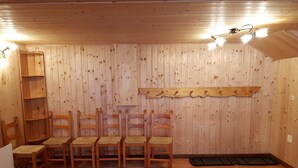 Quarto com paredes de madeira, ventilador de teto e área de estar com quatro cadeiras de madeira e uma pequena prateleira.