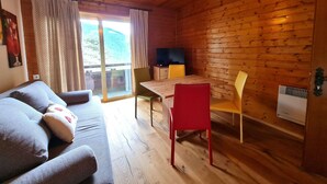 Um quarto aconchegante com teto de madeira, um sofá, uma mesa de jantar com cadeiras e uma televisão.
