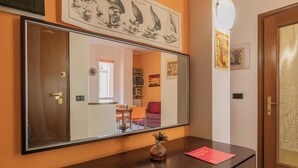 Quarto de hotel com um espelho grande, cómoda de madeira, uma pequena planta e uma placa vermelha sobre a cómoda.