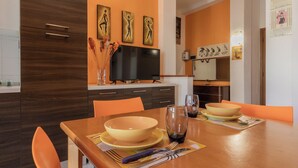 Cozinha moderna com uma mesa de jantar posta para dois, apresentando uma TV de tela plana acima do balcão e um vaso decorativo com flores secas.