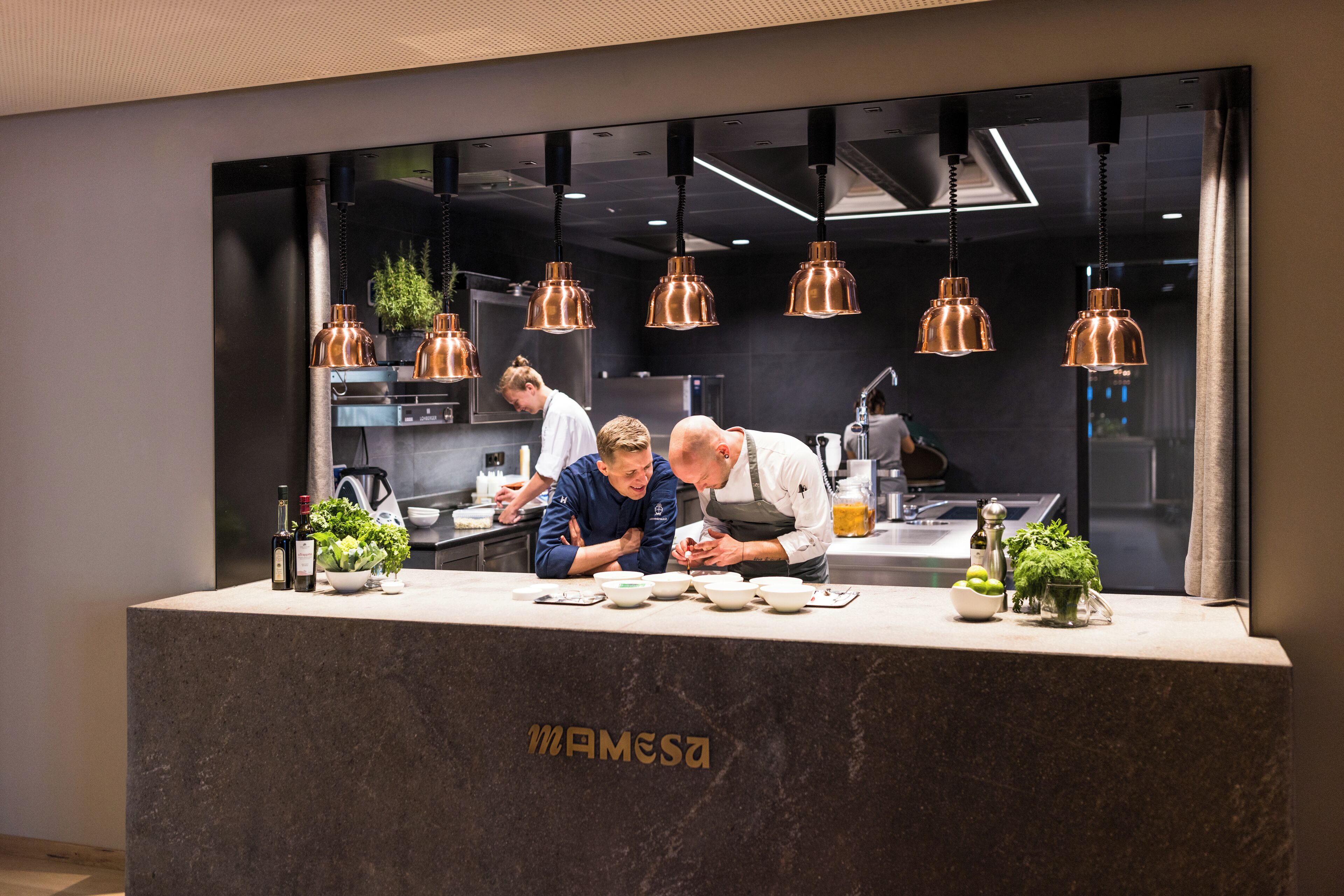Uma cozinha moderna com luminárias pendentes em cobre, bancada de mármore e nome de marca visível.