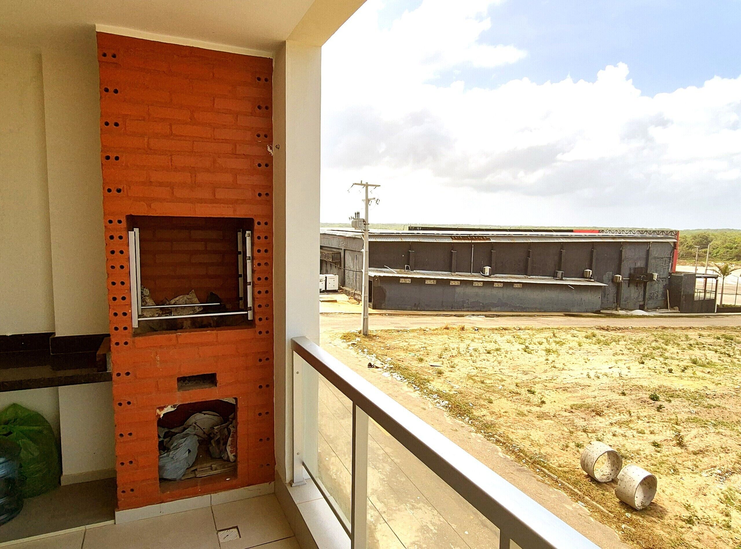 Varanda com parede de tijolos e guarda-corpo de metal, com vista para uma área de construção.