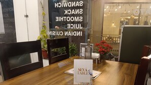 Uma mesa de madeira com uma placa que diz 'SEVA TABLE' e um vaso de planta.