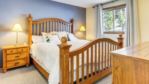 Quarto com cama de madeira, duas mesas de cabeceira, janela com cortinas e vista para o verde lá fora.