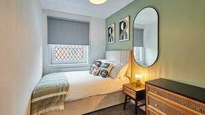 Quarto com cama, mesa de cabeceira, cômoda, janela com persiana e decoração na parede.