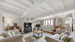Uma sala de estar espaçosa com pé direito alto, lareira e uma janela grande com cortinas.
