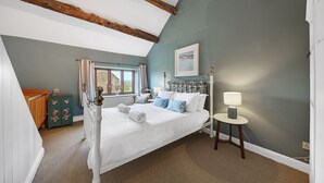 Quarto com cama grande, mesa de cabeceira com luminária, janela com cortinas e cômoda verde.