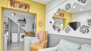 Uma sala de estar moderna com um sofá, uma poltrona e uma cozinha visível por uma porta aberta.