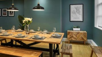 Uma sala de jantar com uma longa mesa de madeira posta para uma refeição, duas luminárias pendentes e um mapa emoldurado na parede.