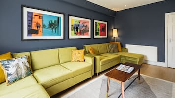 Sala de estar com sofá verde, mesa de centro de madeira e quadros na parede.