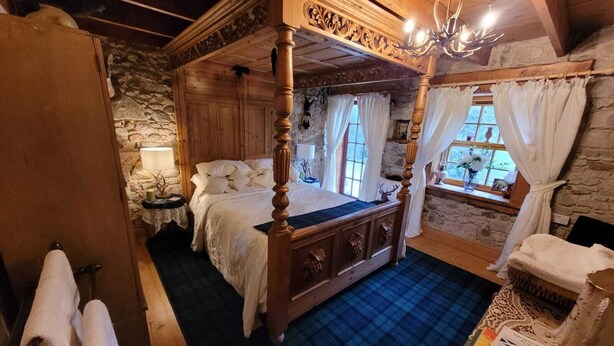Uma cama de dossel tradicional com um painel de parede de pedra, piso de madeira e janela com cortinas.