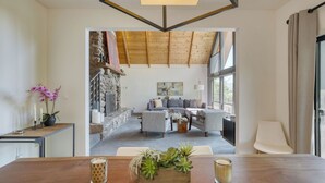 Uma sala de estar moderna com lareira de pedra, uma janela grande e uma área de jantar com mesa de madeira.