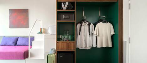 Quarto de hotel com cama, escrivaninha, guarda-roupa e mala.