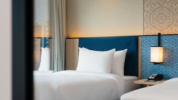 Quarto de hotel com duas camas, uma mesa de cabeceira com abajur e parede com padrão.