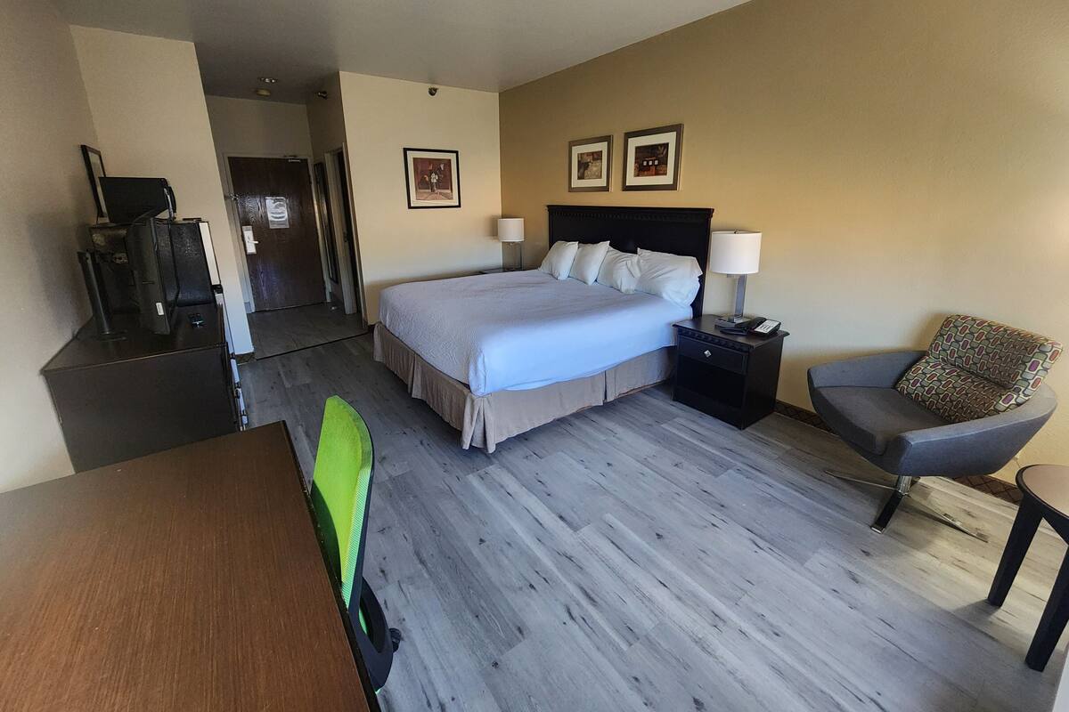 Quarto de hotel com cama, mesas de cabeceira, uma cadeira, escrivaninha e televisão.