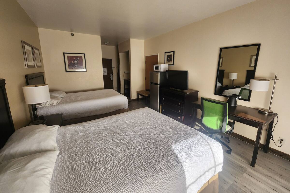 Quarto de hotel com duas camas, uma escrivaninha com computador, televisão, micro-ondas e espelho.
