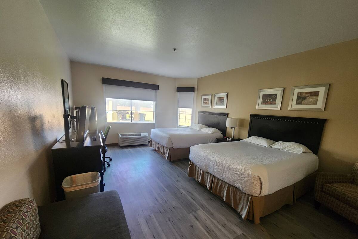 Quarto de hotel com duas camas, uma escrivaninha, uma cadeira e uma janela.