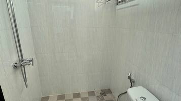 Uma casa de banho pequena com chuveiro, sanita e toalha no assento.