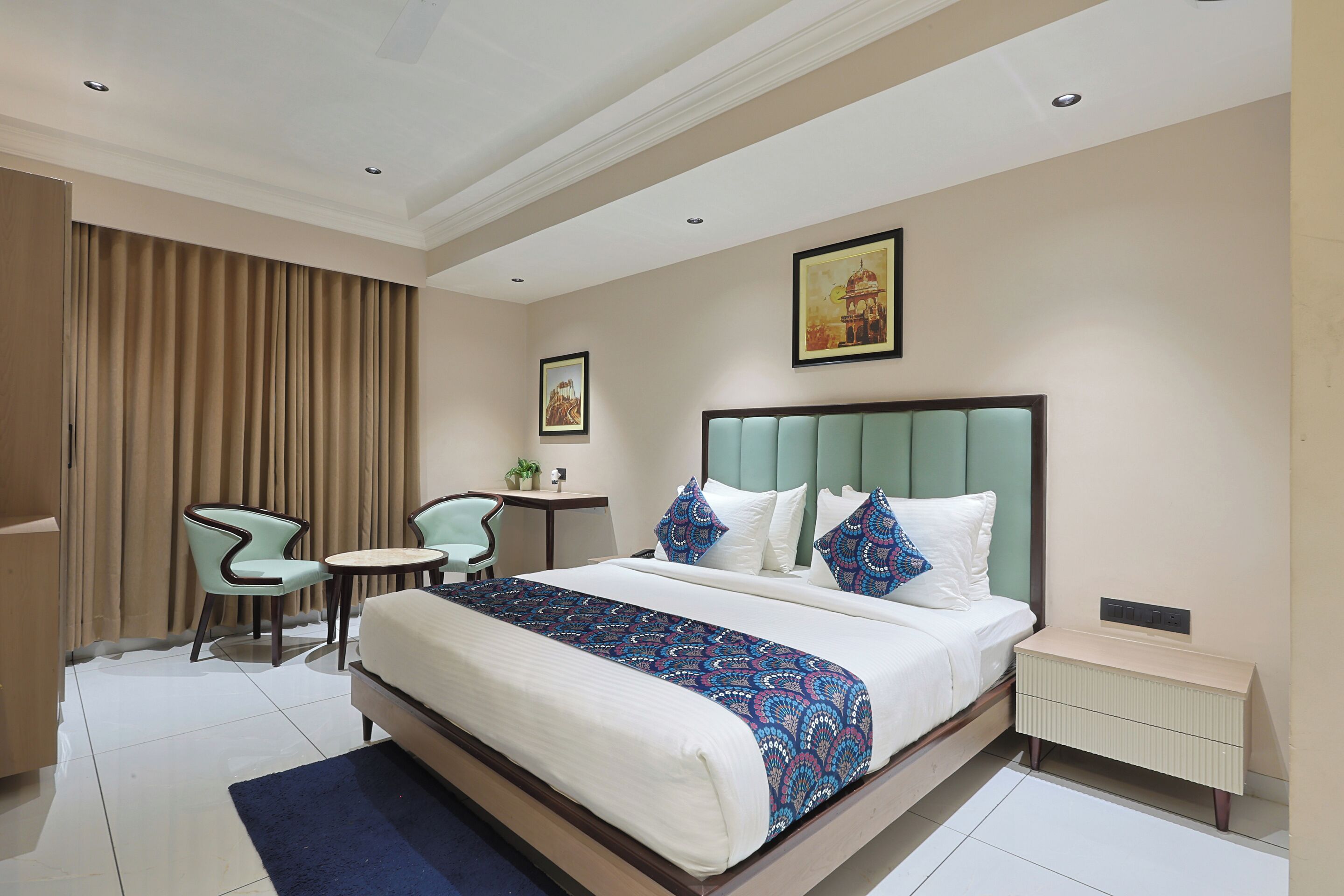 Quarto de hotel com uma cama grande, uma escrivaninha, duas cadeiras e uma mesa de cabeceira.