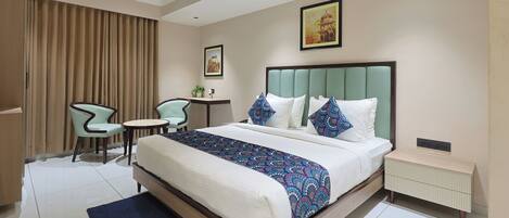 Quarto de hotel com uma cama grande, uma escrivaninha, duas cadeiras e uma mesa de cabeceira.