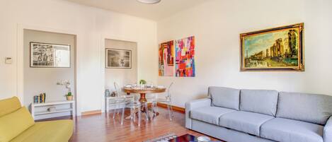 Uma sala de estar moderna com um sofá, uma mesa de centro com livros, um espaço de refeições com mesa e cadeiras, e obras de arte nas paredes.