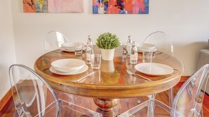Mesa de jantar redonda com cadeiras transparentes, uma planta em vaso no centro e um vaso de vidro.