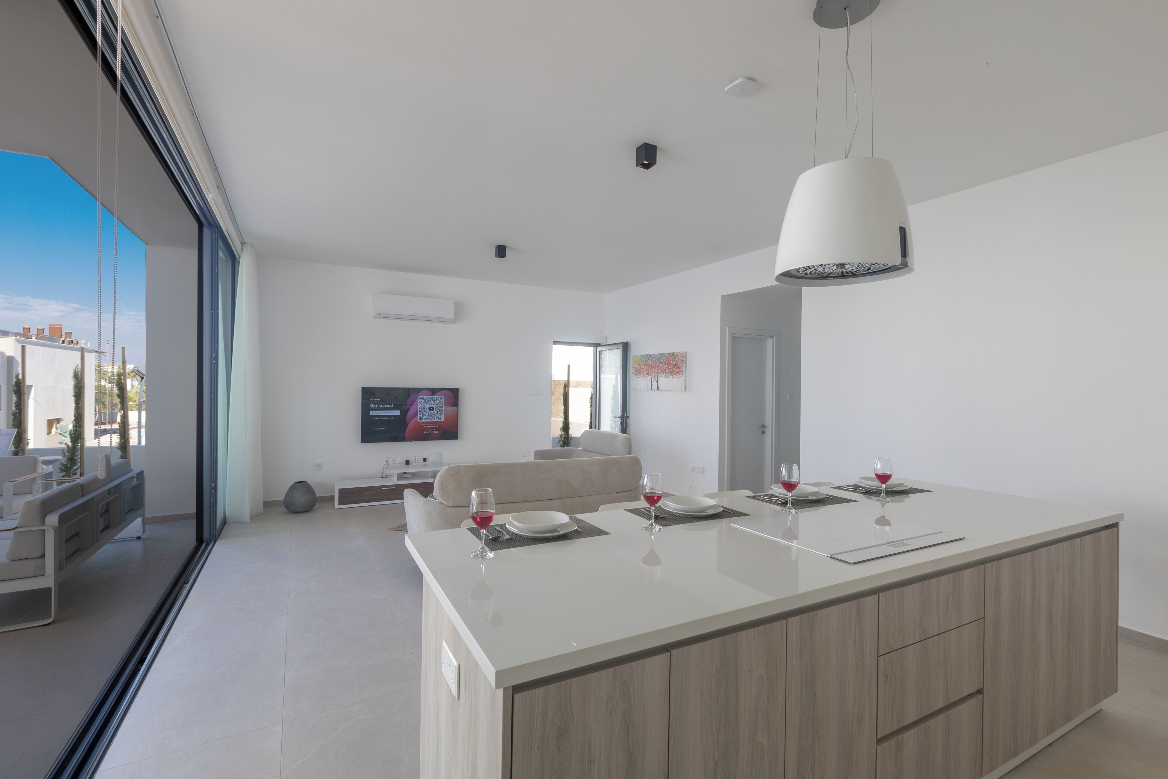 Uma cozinha moderna com uma ilha grande, uma área de refeições com um sofá e uma TV ao fundo.