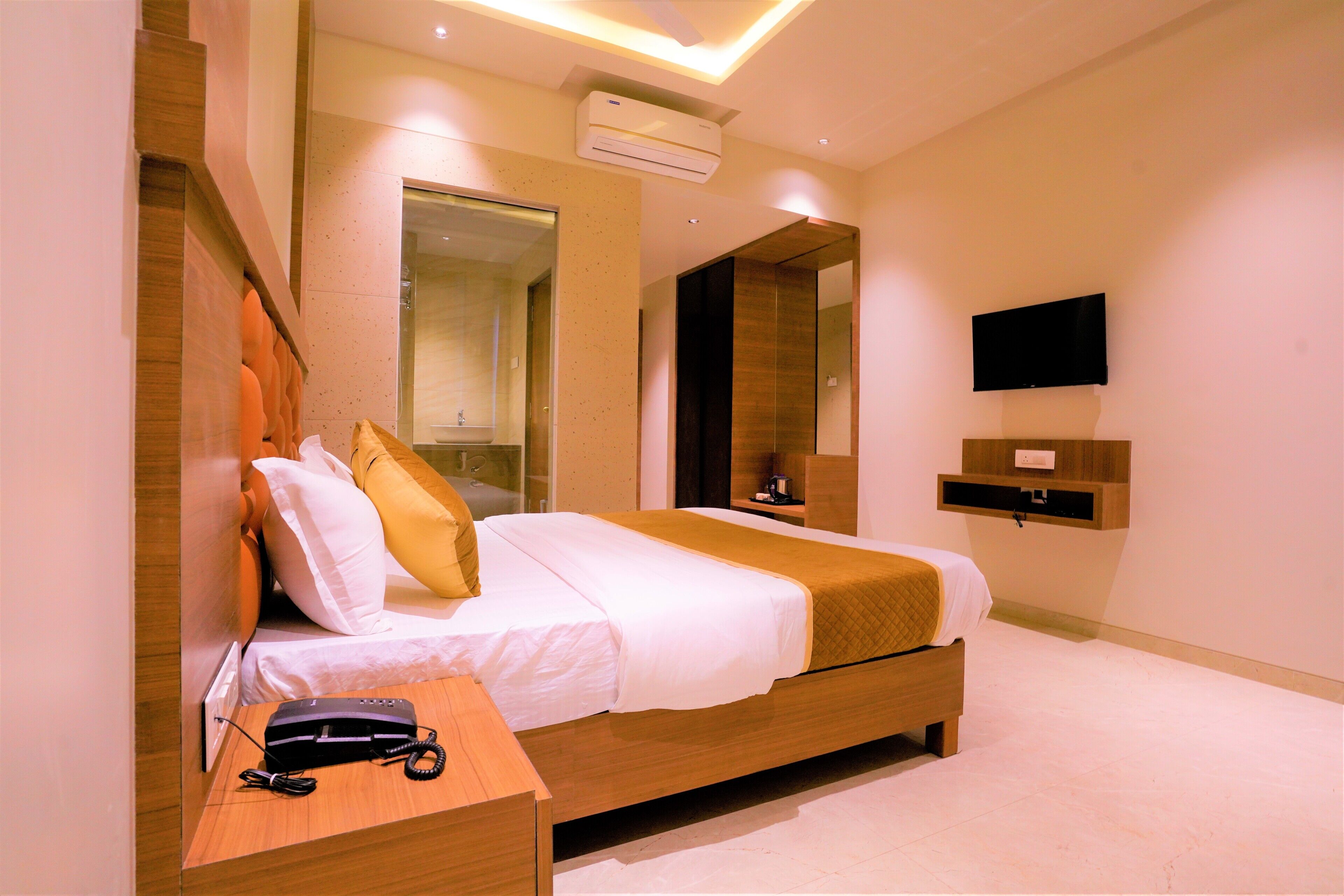 Quarto de hotel moderno com uma cama grande, mesa de cabeceira com telefone, espelho e televisão na parede.