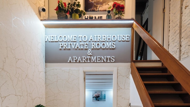 Uma área de recepção com uma placa para Airhouse Private Rooms & Apartments, uma escadaria e uma visão rápida de um quarto com uma cama e uma janela.