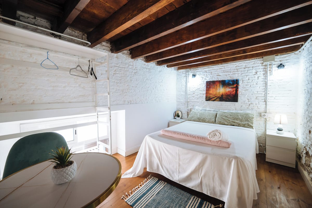 Quarto com cama, mesa de cabeceira, luminária, quadro, planta e uma cadeira.